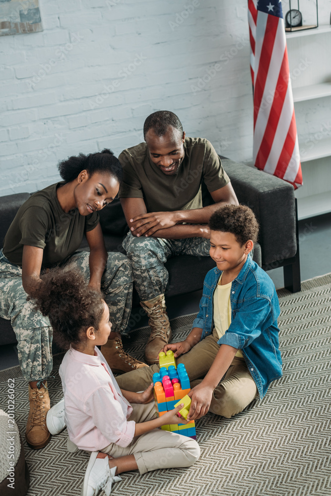 Woman and man in army uniform looking at their children playing with ...