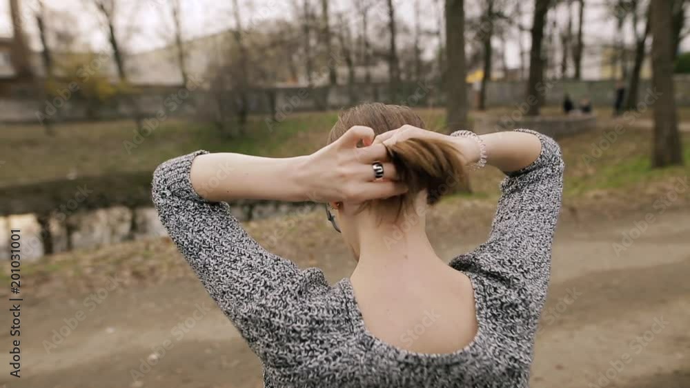 Woman tying her smooth hair in ponytail, making hairdo, back view ...