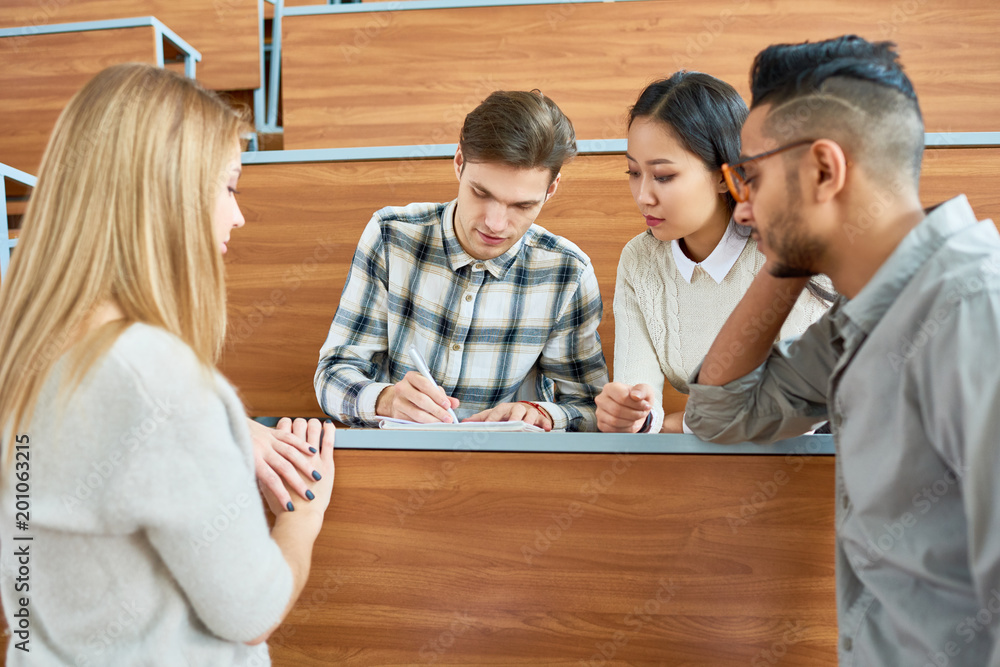 Group of international students sitting around desk in modern lecture ...