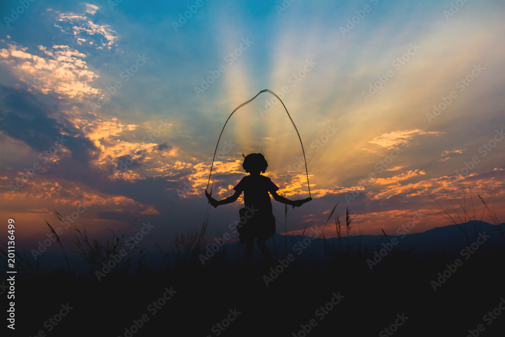 Silhouette of little girl jump rope on mountain at sunset, summer time ...