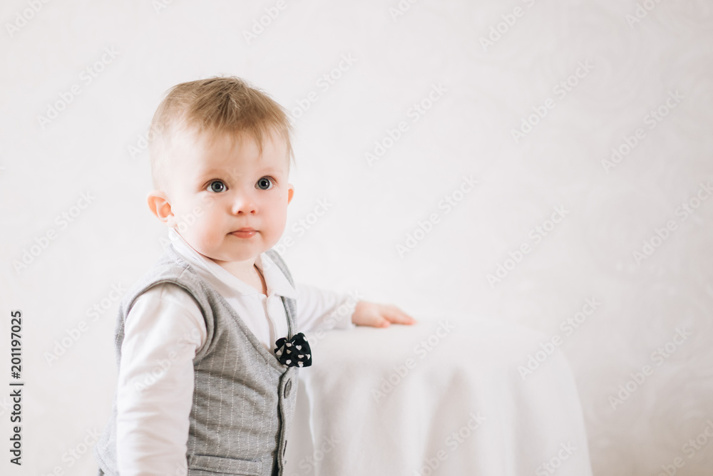 Happy cute boy in a gentleman's suit stands near the support on a light ...
