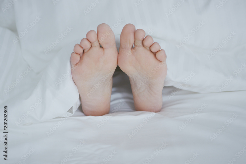Crop shot of woman lying under cozy white blanket in bed sticking out ...