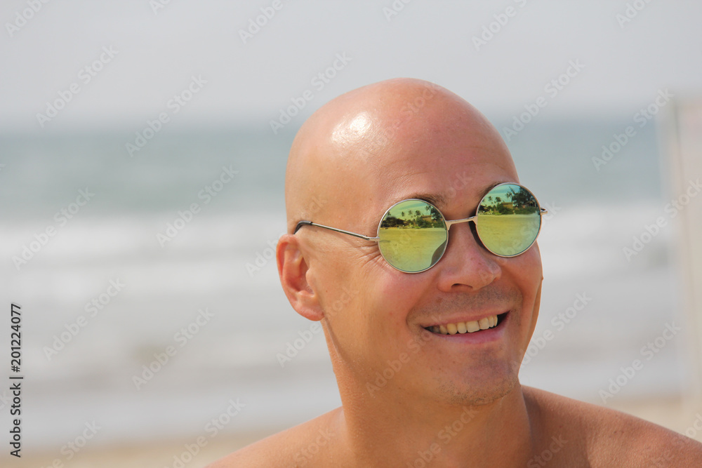 Bald man in mirror sunglasses. A beautiful tanned man on vacation ...