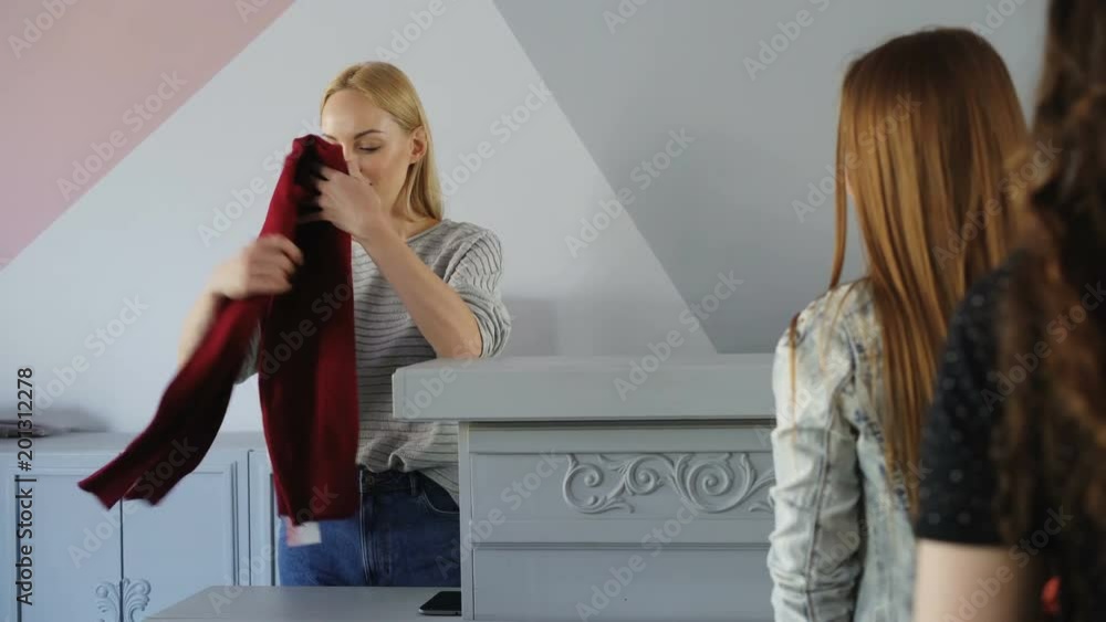 Friendly female cashier is taking garment from customer standing in ...