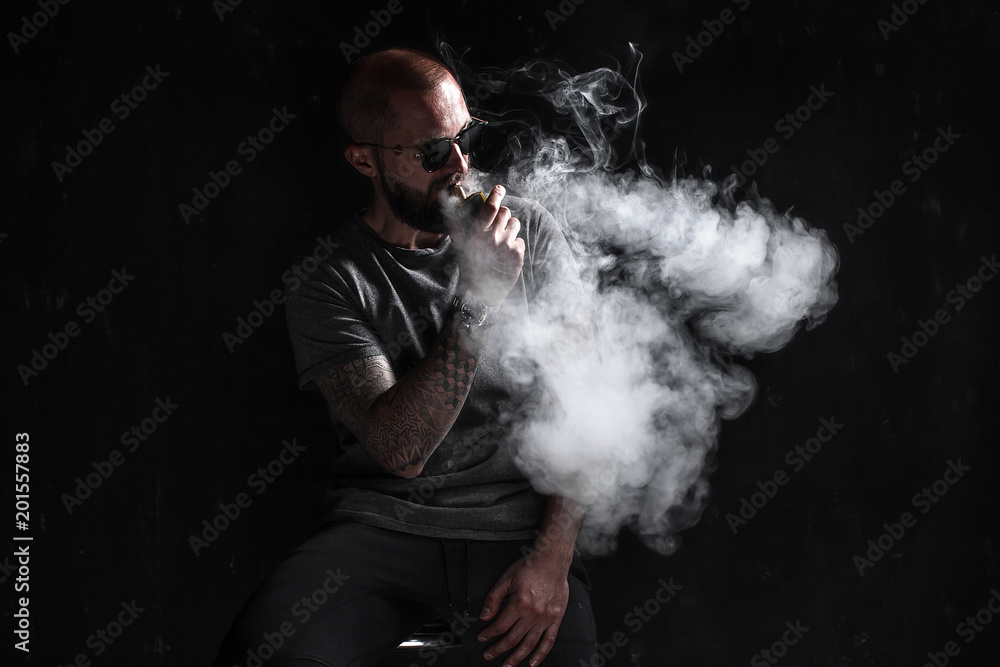 Men with beard in sunglasses vaping and releases a cloud of vapor on ...