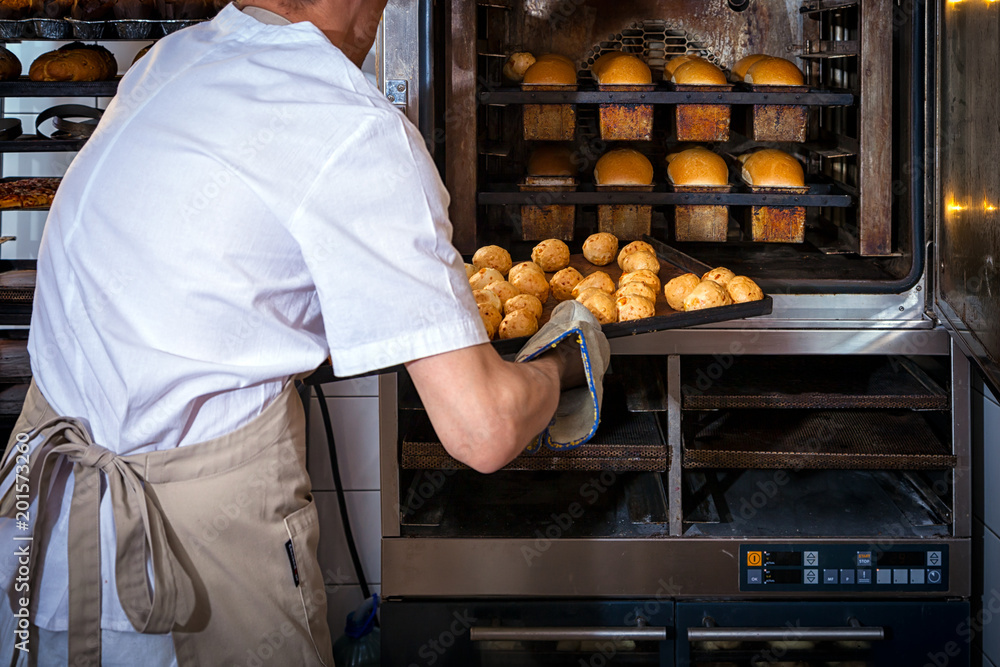 A male baker in white uniform and a beige apron bakes bread and takes ...