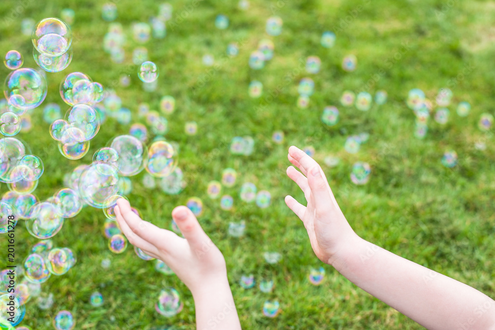 Kids hands catching bubbles with fresh green grass at a background ...
