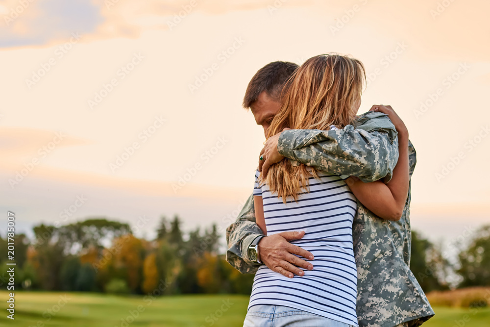 Soldier is hugging a woman outdoor. Reunion of a couple in the evening ...