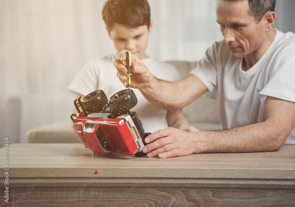 Serious man is fixing a wheel of toy car by tool with concentration ...