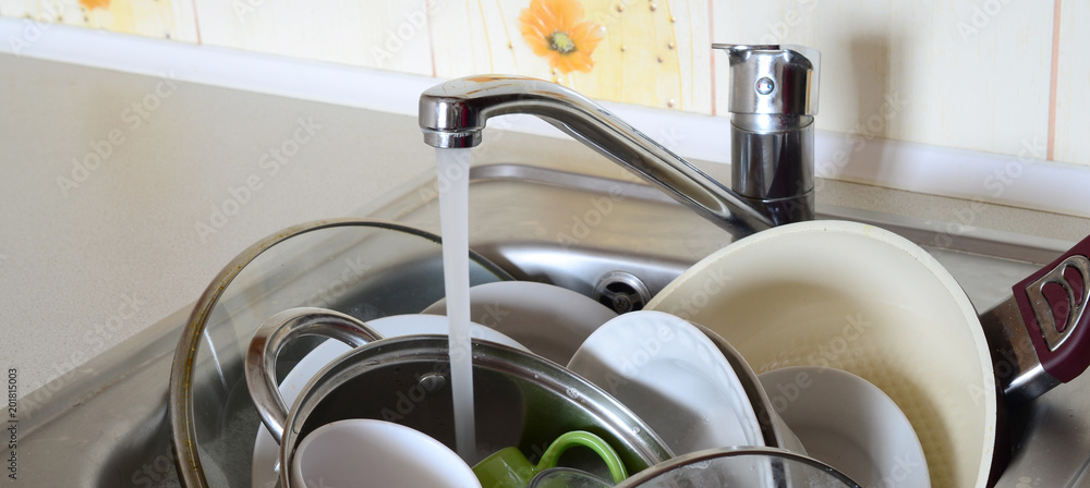 Dirty dishes and unwashed kitchen appliances lie in foam water under a ...