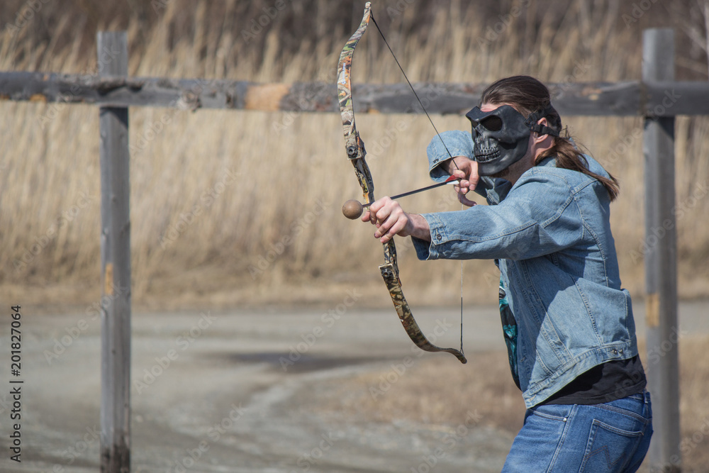 Archer man in skull mask with bow aim at something in front of him ...
