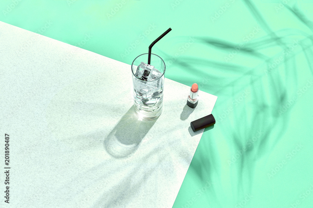 High angle view of lipstick and drinking glass with ice on table. Blue ...