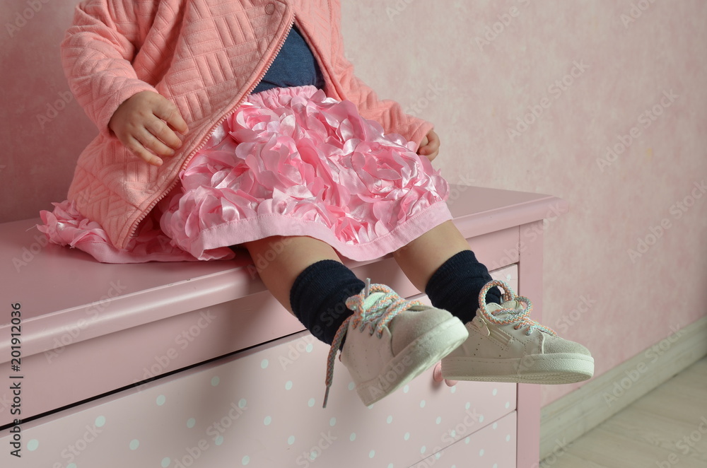 Legs of a little girl sitting on a dresser. close-up shot of the baby's ...