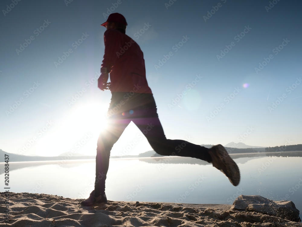 Tall fit man running fast by the sea on the beach. Powerful runner ...