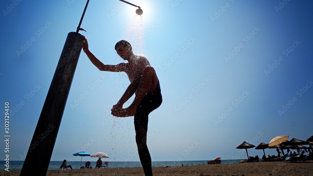 Silhouette man showering his body on beach shower against sun Stock ...