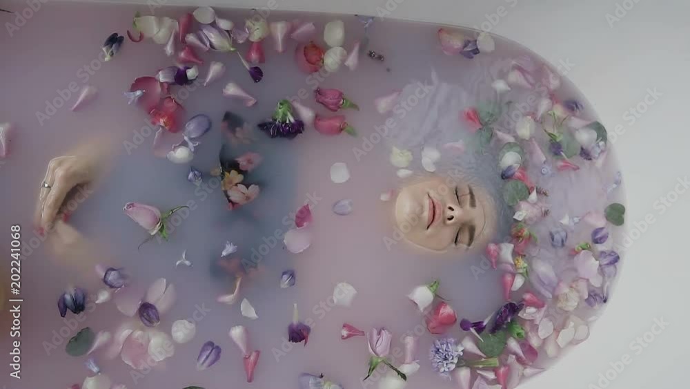 Attractive girl bathing in milk bath filled with fragrant flowers of ...