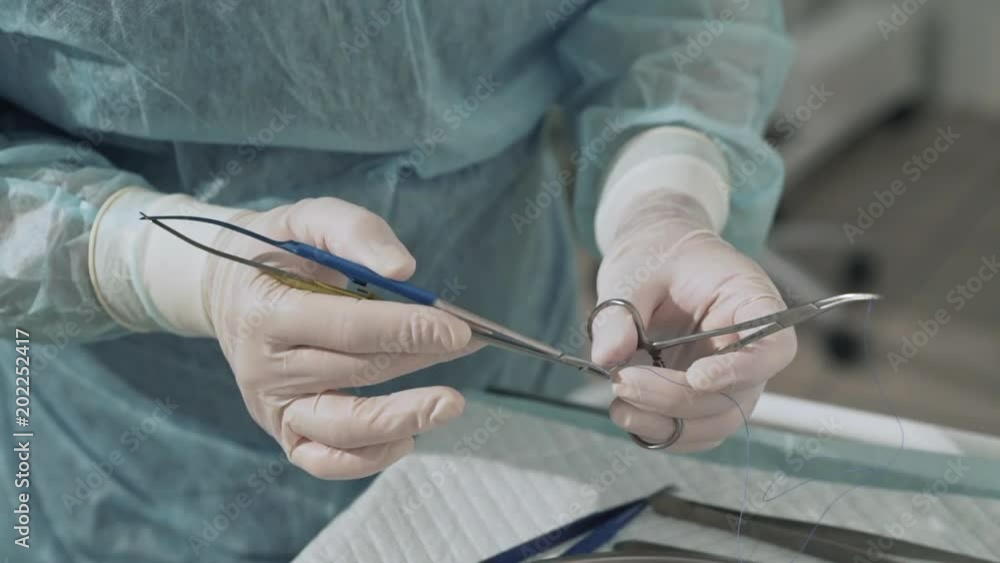 Closeup, the surgeon holds a clamp with a surgical needle in his hand ...