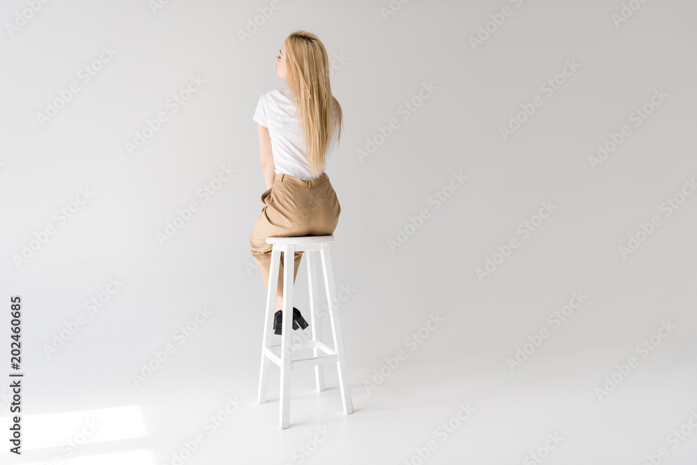 back view of stylish blonde woman sitting on stool on grey Stock Photo ...