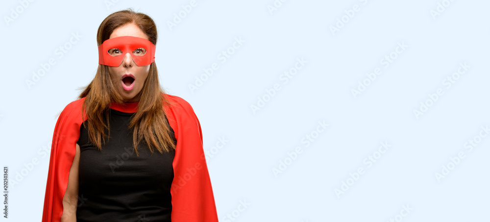Middle age super hero woman wearing red mask and cape scared in shock ...