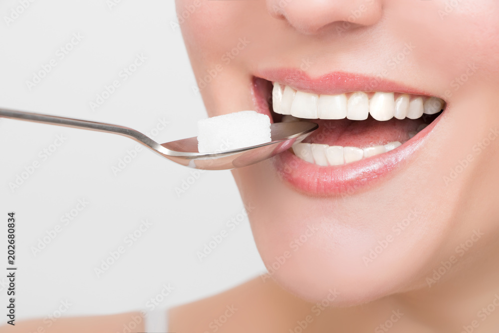 Beautiful woman with white teeth leads a spoon with sugar cubes in her ...