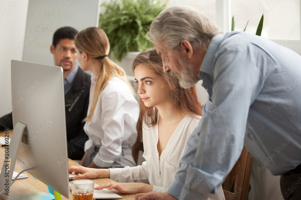Aged executive manager boss checking work of young trainee looking at ...