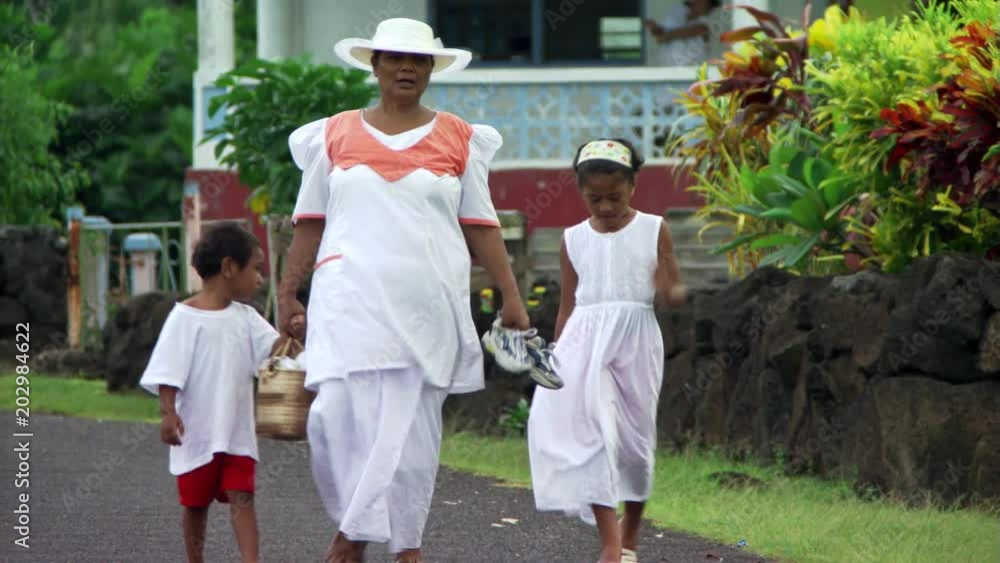 Samoan woman walking with two children along a paved neighborhood ...
