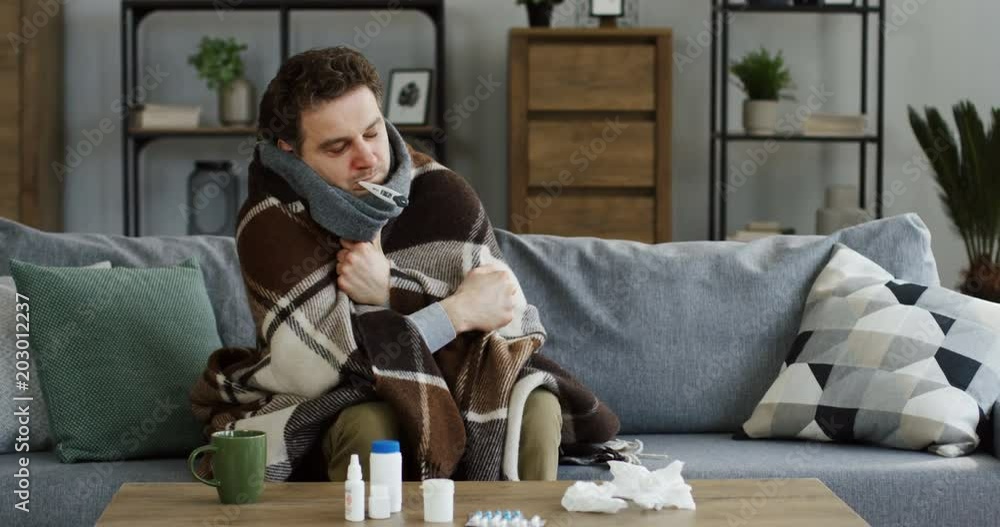 Unwell caucasian man covered with a warm plaid measuring a temperature ...