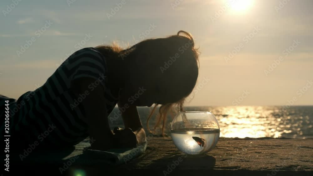 lying on the seaside little girl looking fishbowl with a small fish ...
