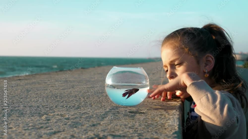 playful cute little girl looking at fish in fishbowl playing with her ...