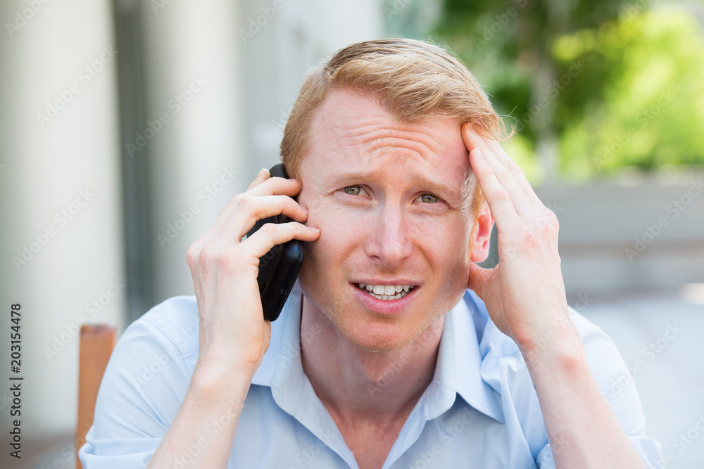 Closeup portrait, worried young man in blue shirt talking on phone to ...