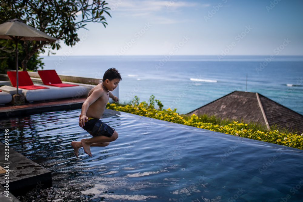 Asian boy taking body up to jumps into swimming pool with beautiful ...