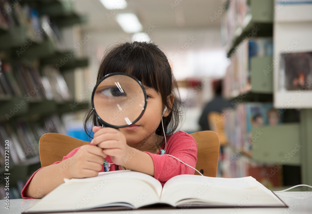 Little girl child looking through a magnifying glass in the library ...