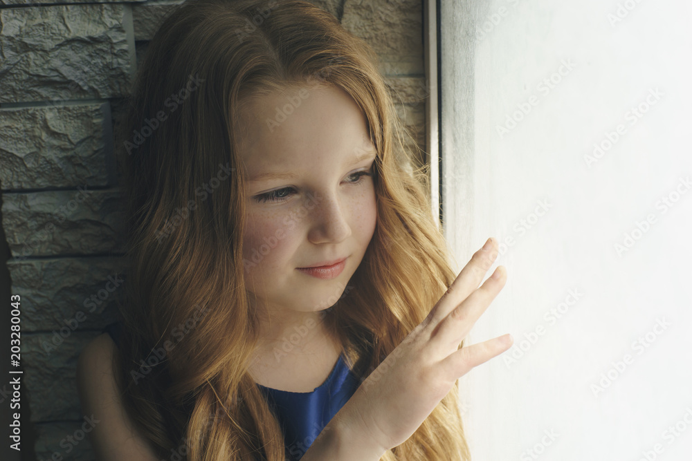 Beautiful little girl smiling and watching out the window. A child ...