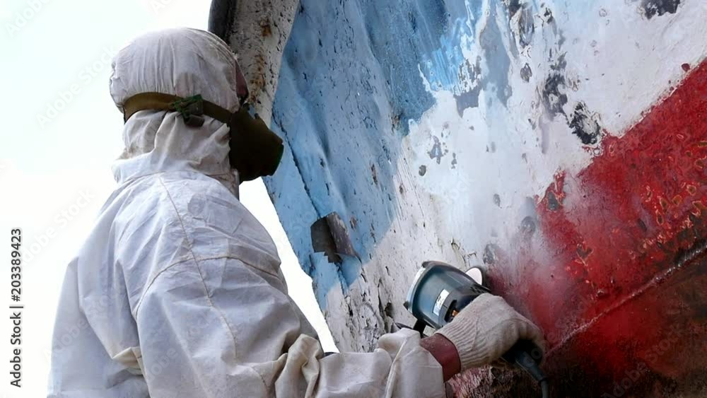 Working people tear off paint on metal in repairs process at shipyard ...