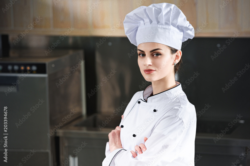Professional female chef standing with arms folded on modern kitchen ...