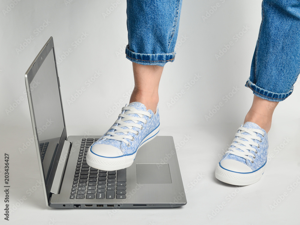 Female foot in jeans and sneakers comes with a foot on the laptop on a ...