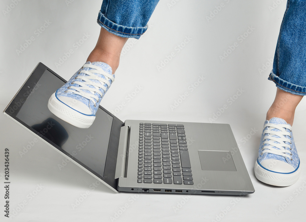 Female foot in jeans and sneakers comes with a foot on the laptop on a ...