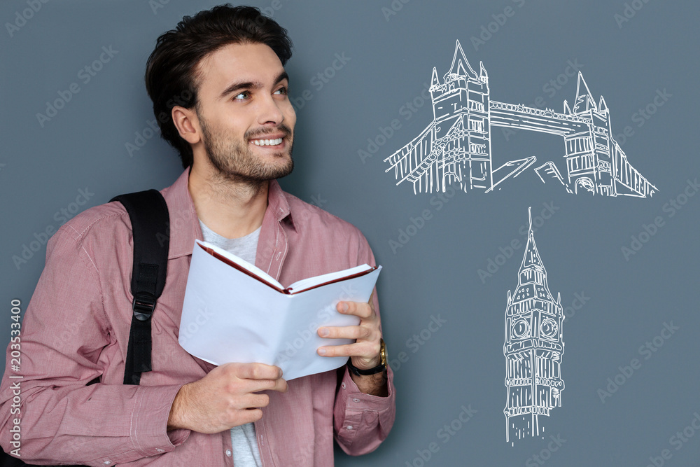Pleasant dreams. Cheerful dreamy student standing with a book in his ...