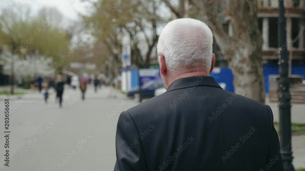 A striking back view of a wise old man in his 80s strolling along a ...