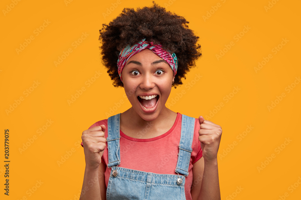 Portrait of overjoyed female clenches fists with happiness, opens mouth ...