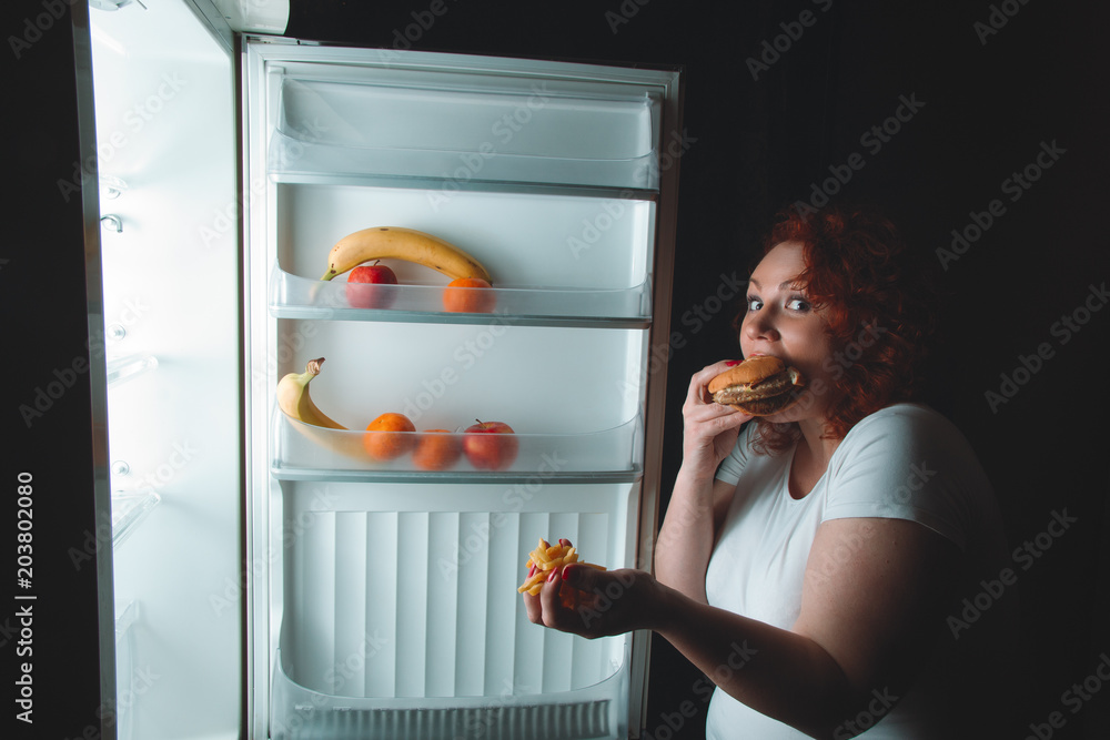 Big woman eat fast food. Red hair fat girl looking inside refrigerator ...