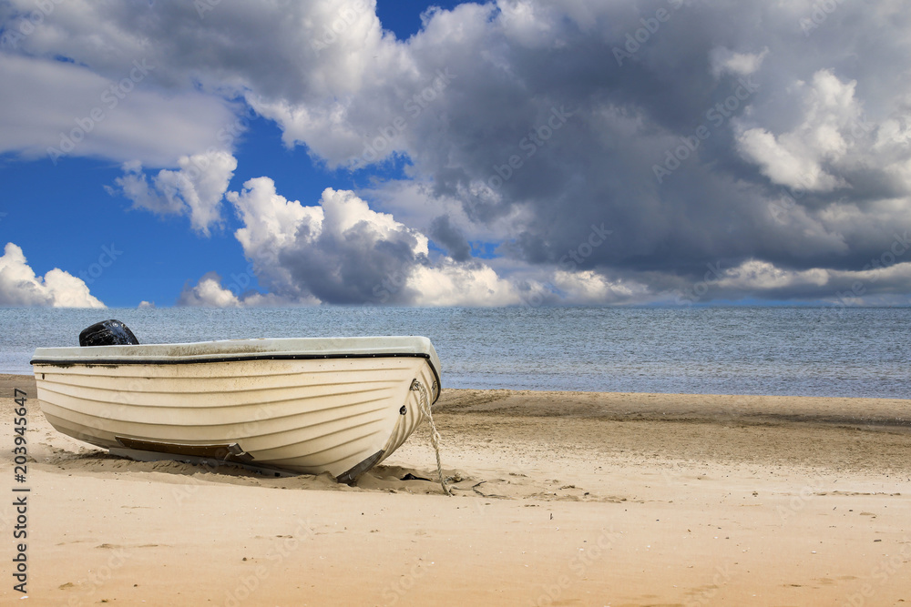 Einzelnes weißes Boot am Strand an der Ostsee im Hintergrund dunkle ...