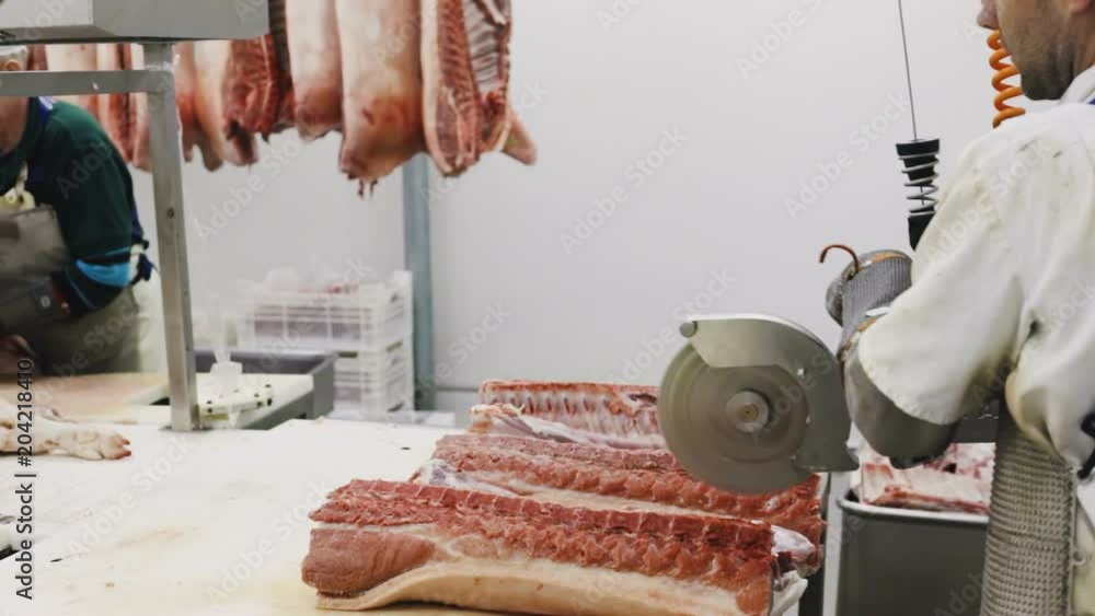 male butcher employee in uniform cuts meat by electric saw factory ...