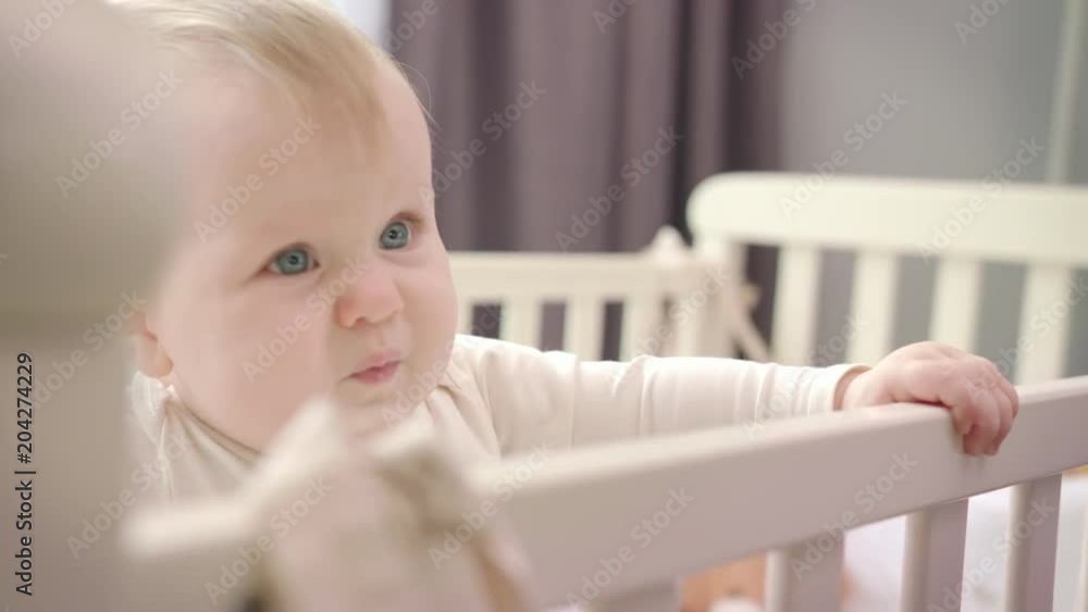 Sad baby standing in bed. Unhappy child holding on bed. Little baby ...