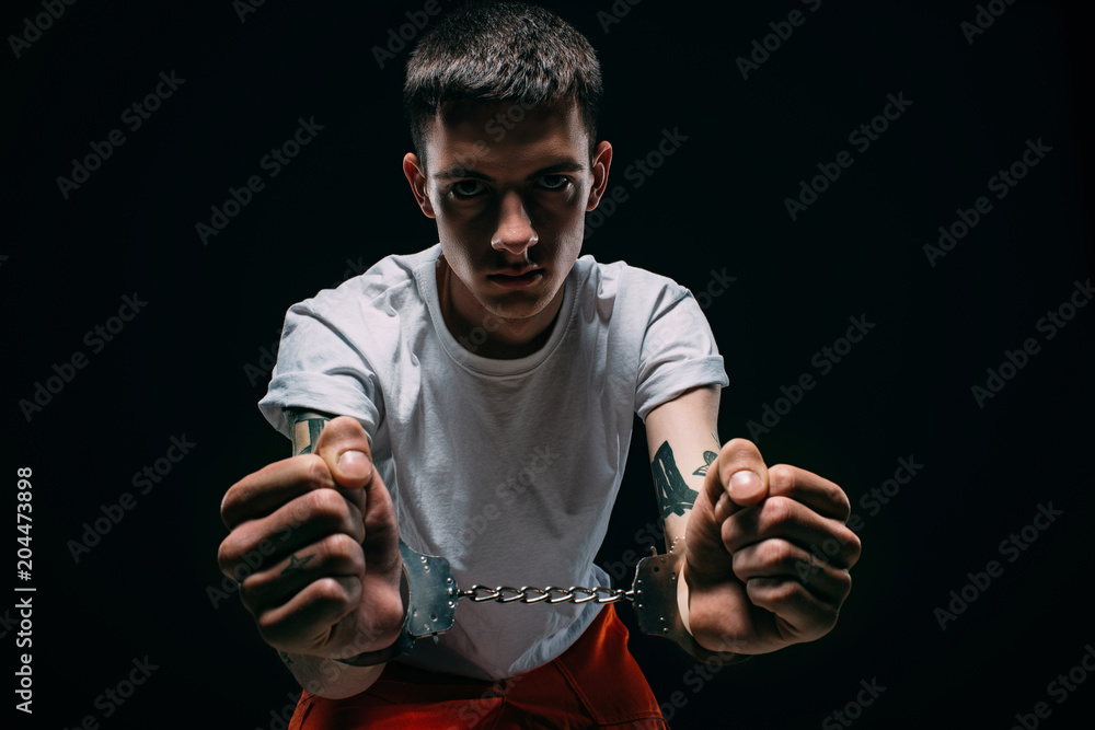 Sad man in prison uniform showing cuffs on dark background Stock Photo ...