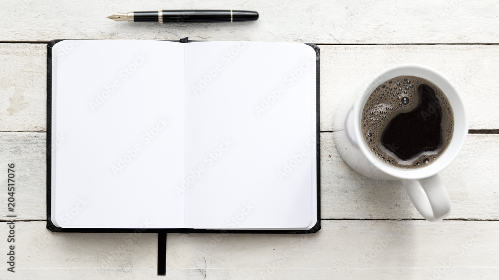Notebook on a white wooden table next to a pen and some coffee in a mug ...