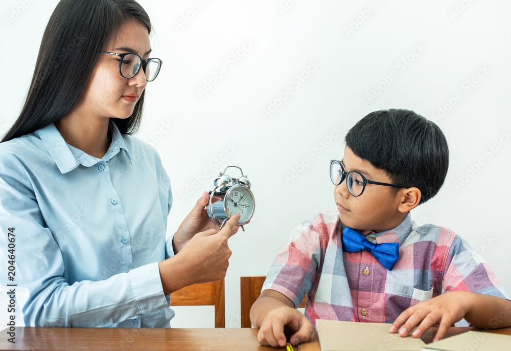 Portrait of school boy looking at clock, teacher displays the clock to ...