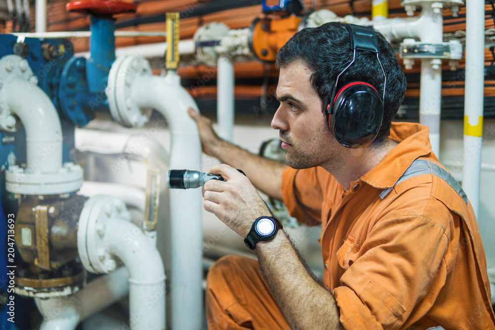 Marine engineer inspecting ship's engine with torchlight in engine ...