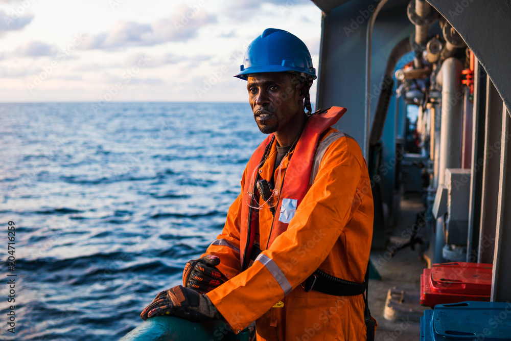 Tired rating Seaman AB or Bosun on deck of vessel or ship , wearing PPE ...