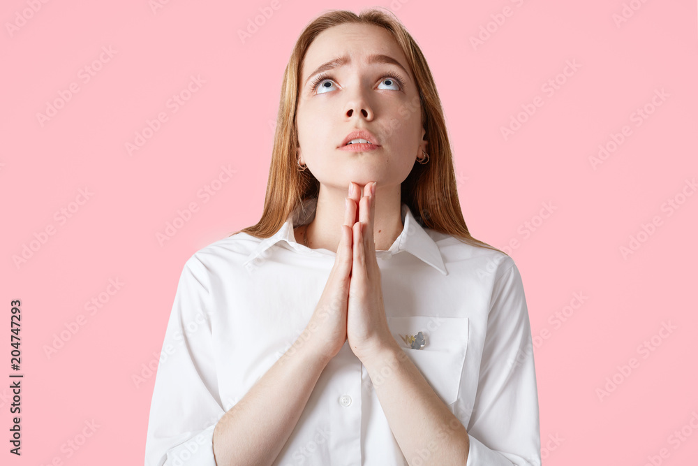 Horizontal portrait of hopeful female keeps palms pressed together, has ...